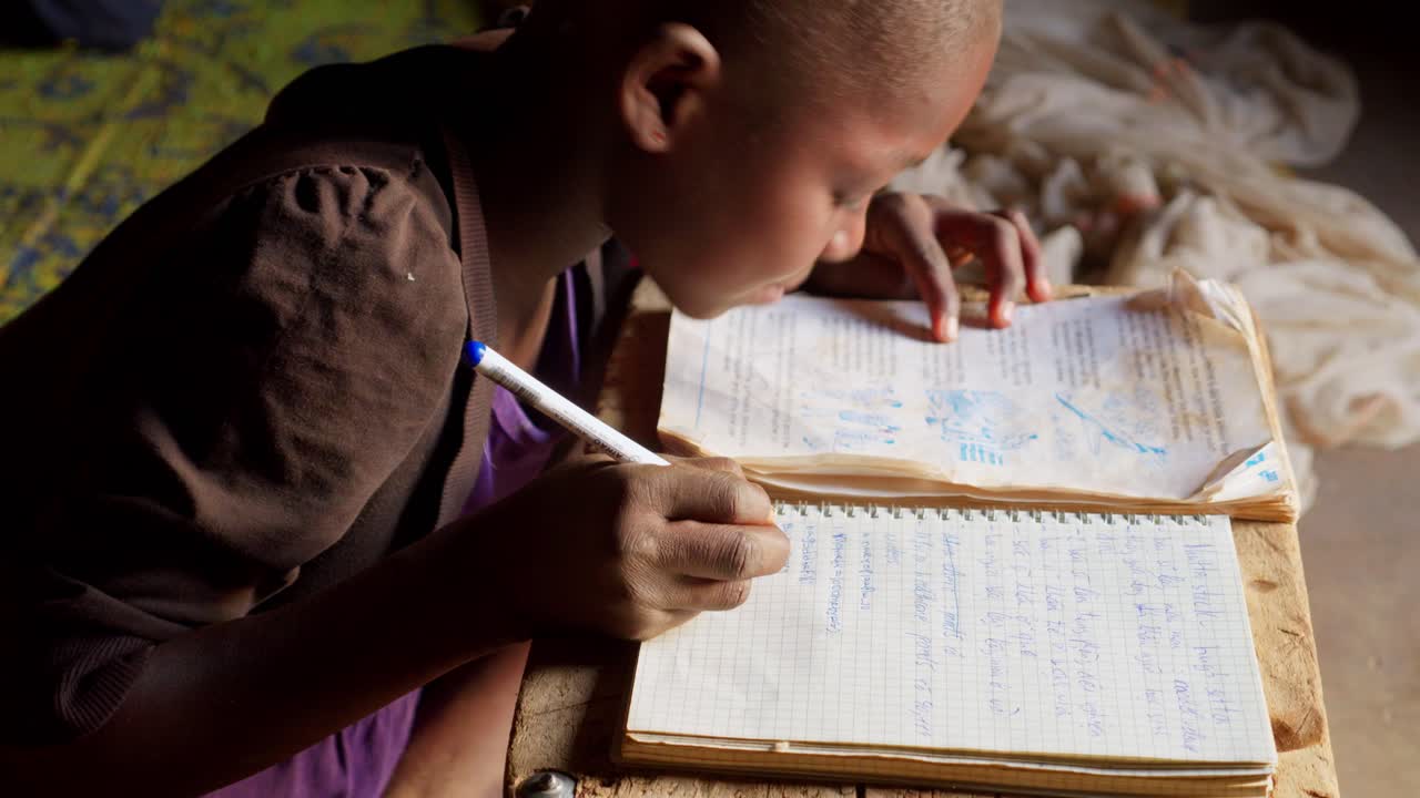 Closeup Shot Of Rural African Boy Writing Down Notes On His Notebook In ...