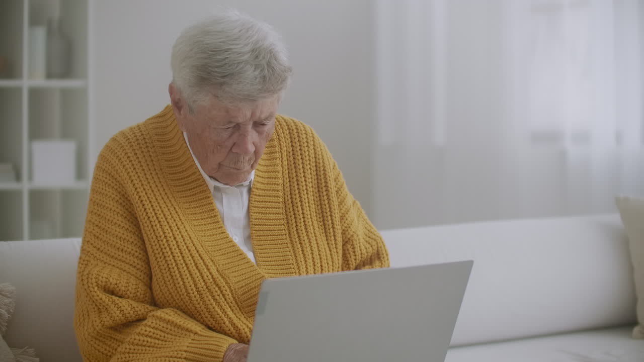 An elderly woman sitting on the couch prints a message on the keyboard ...