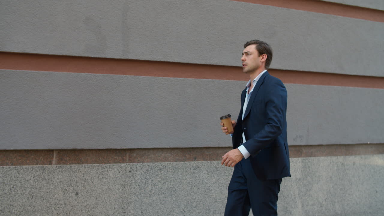 Serious man walking with coffee at street. Man going to meeting with ...
