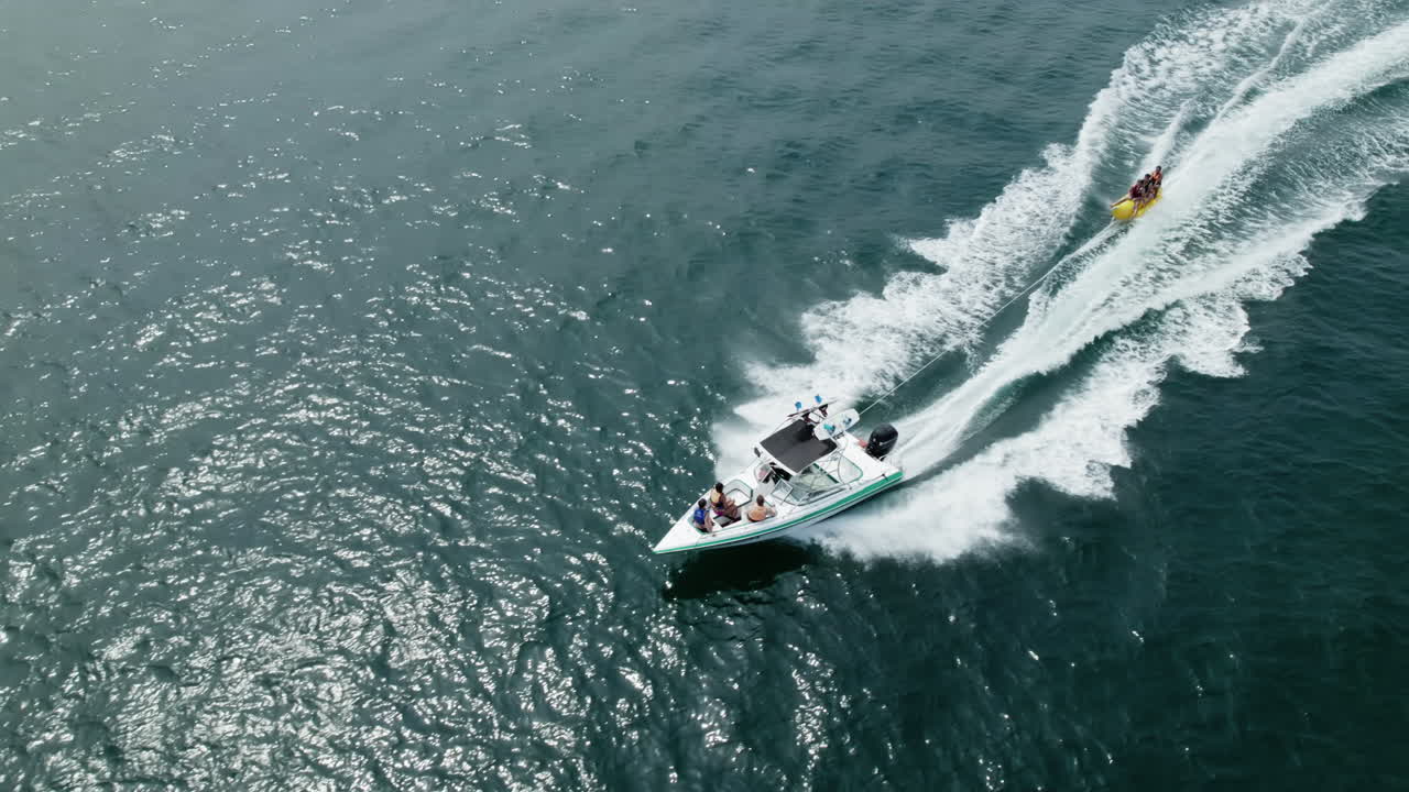 Aerial view of motor speed boat pulls rubber raft with water skiier ...