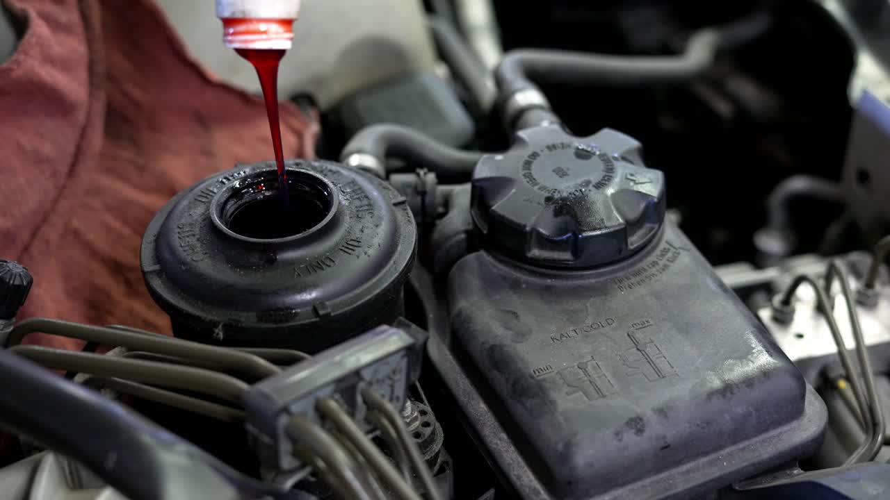 Mechanic slowly pouring red gloopy power steering fluid into car engine ...
