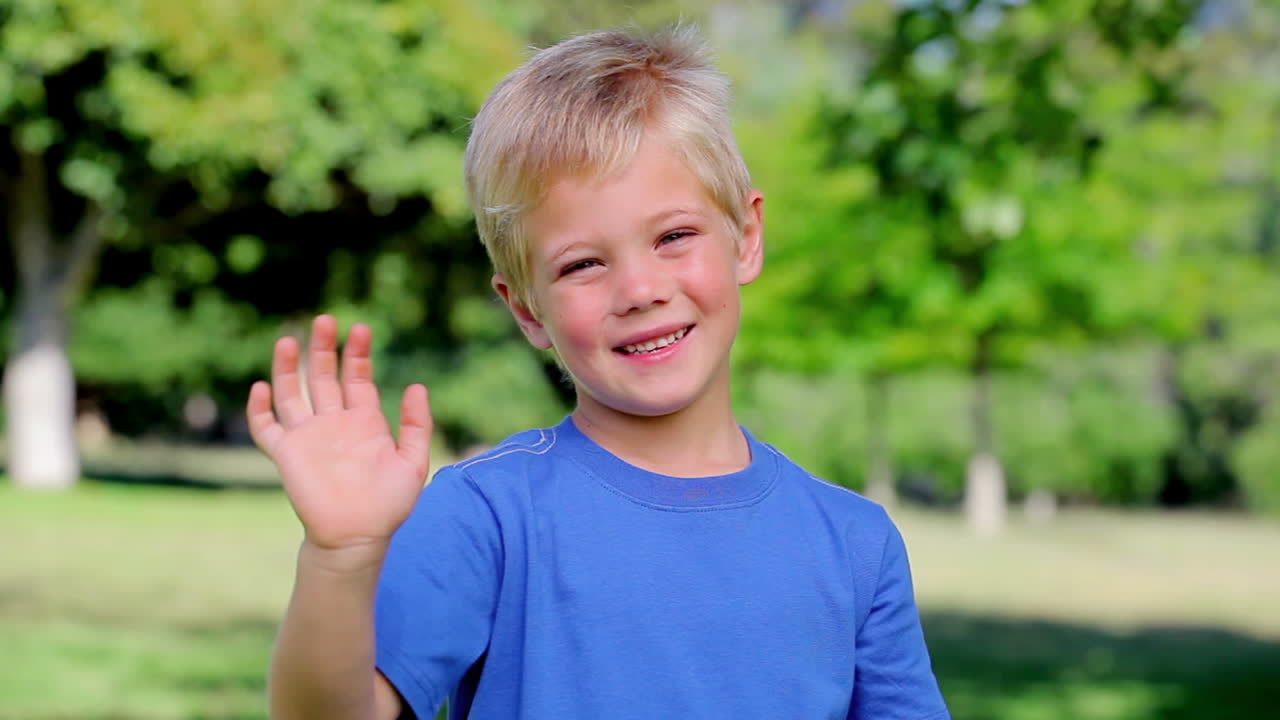 Boy waving towards the camera while smiling | Premium Stock Video Footage