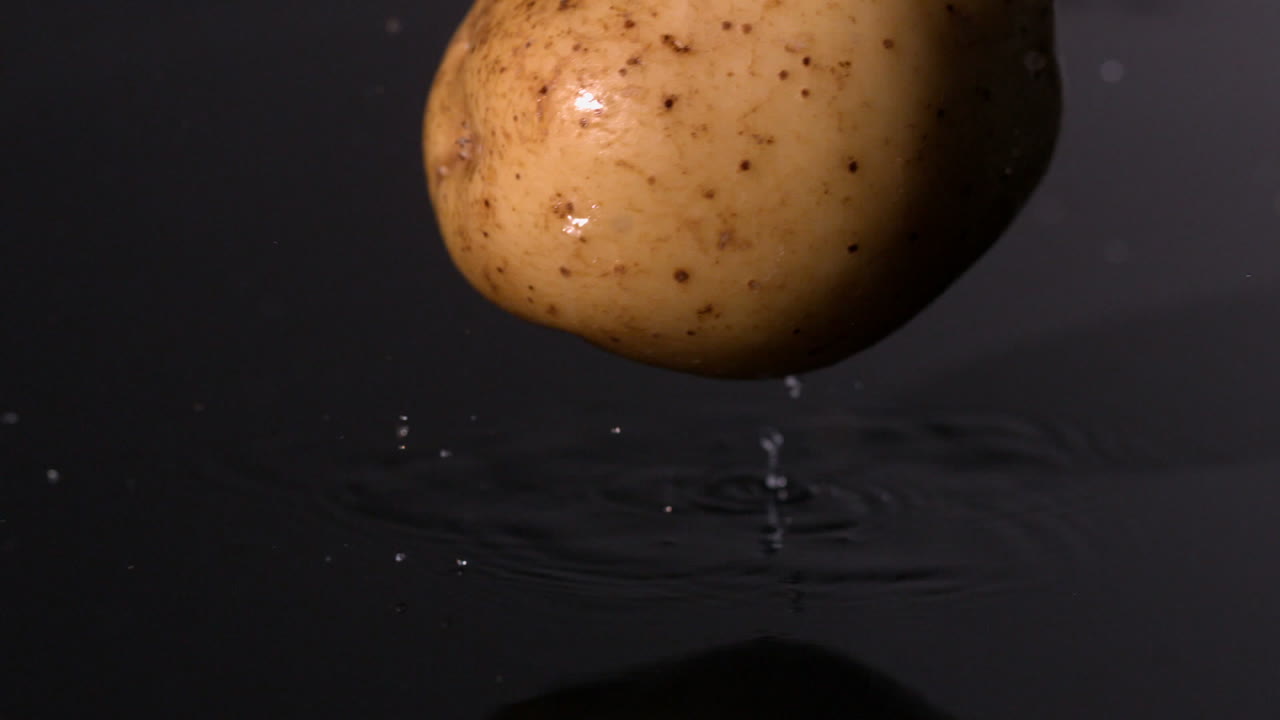 Premium stock video - Potato falling on wet black background
