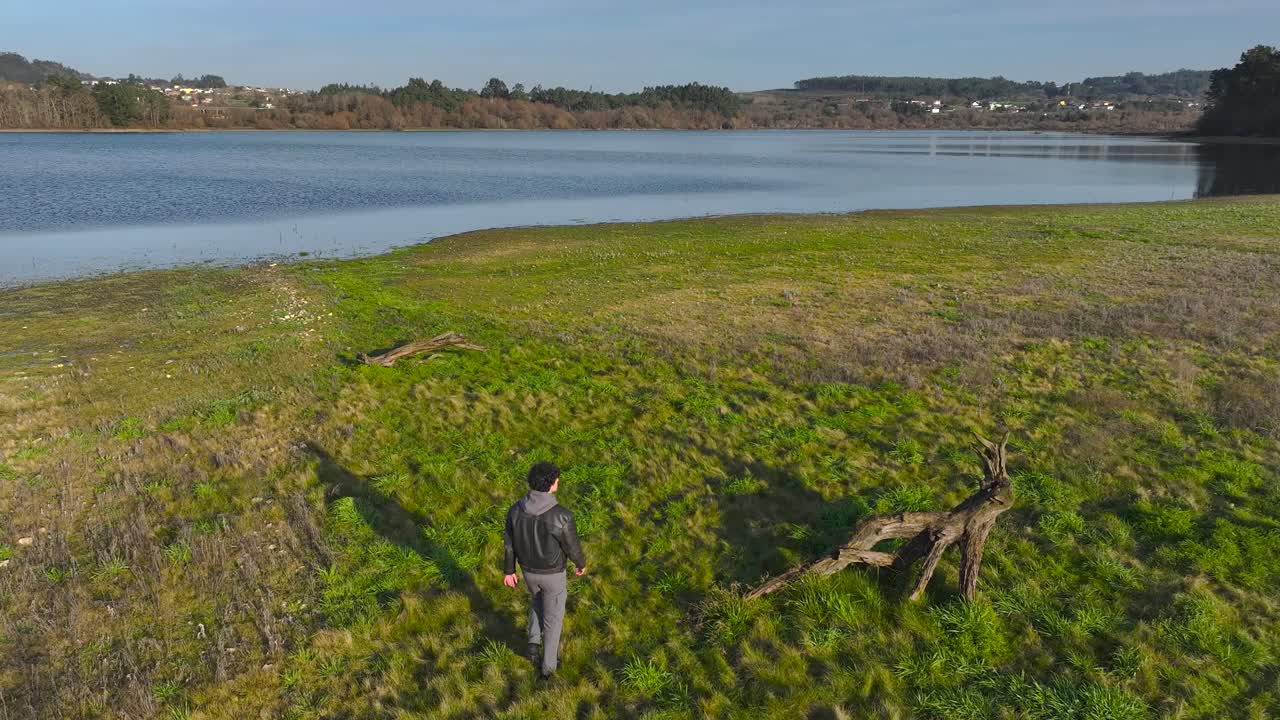 Premium stock video - Aerial view of a man walking through the meadows by the lakeshore