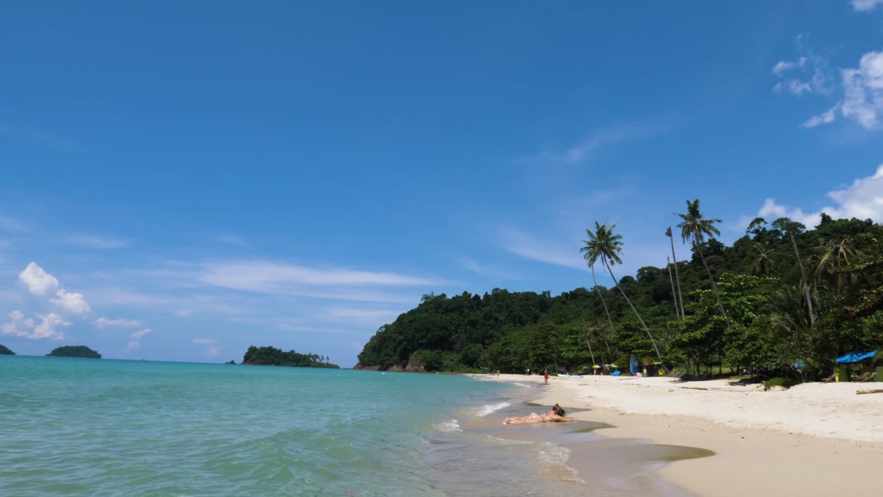 Wide shot of a tropical beach area with two women in bikinis lying on ...