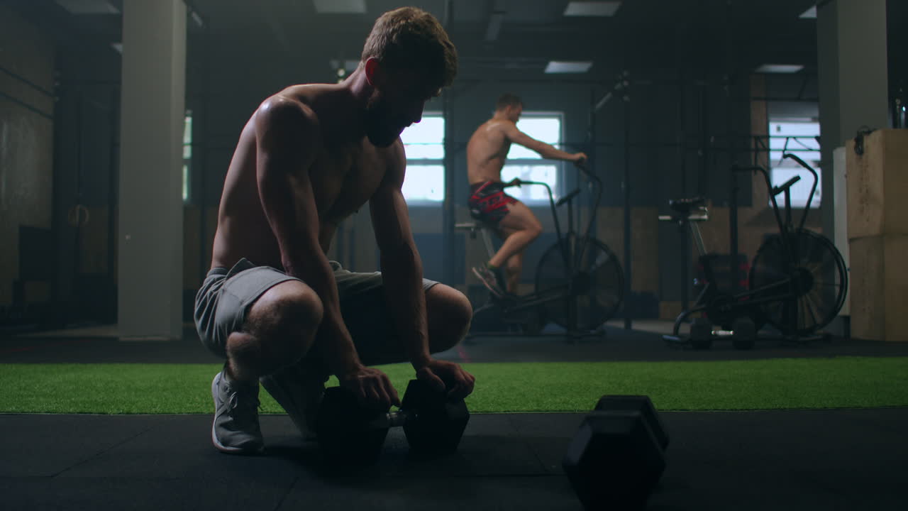 A male bodybuilder after a circular cardio workout sits on the floor of ...