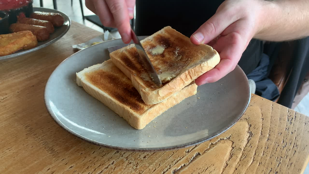Premium stock video - A man buttering toast in a cafe restaurant at breakfast using a knife