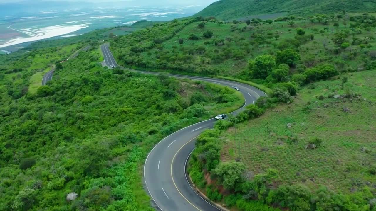 Drone view of a highway with cars driving through the green hilly area ...