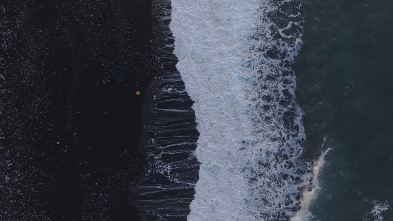 Top view of man running away for waves at black sand beach, aerial ...