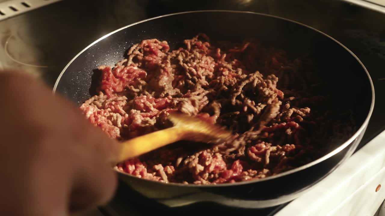 Person cooking ground meat in a pan on a stove, stirring it with a ...