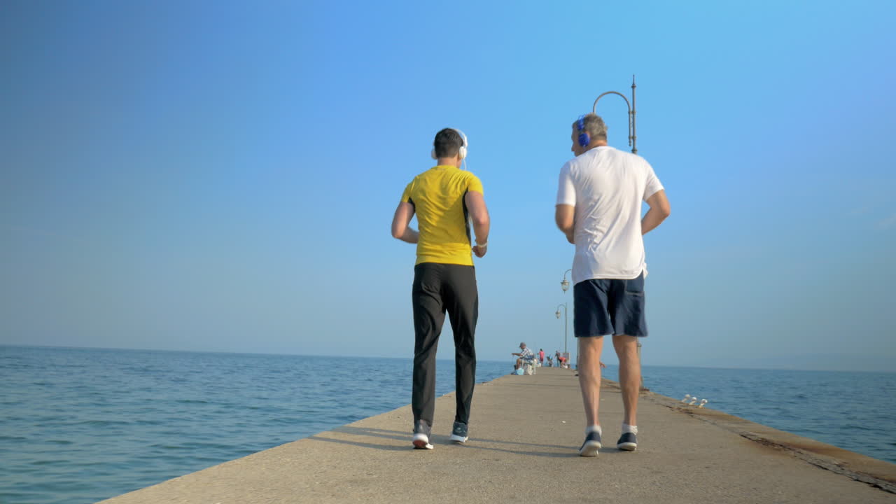 Premium stock video - Men exercising by walking backward along the pier