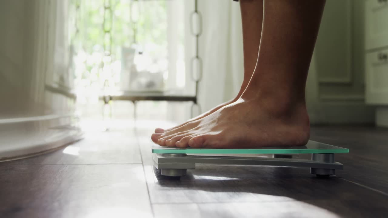 Premium stock video - Woman checking her weight on weighing scale at ...