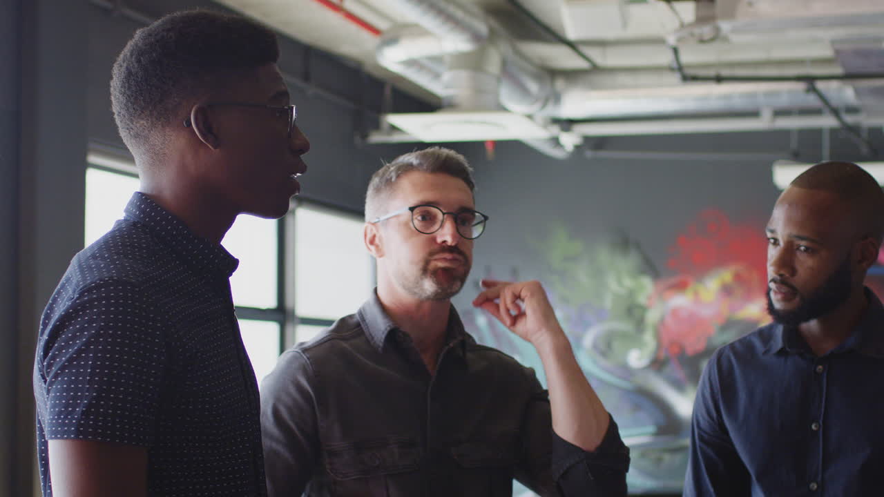 Three millennial male creatives stand having a discussion in their ...