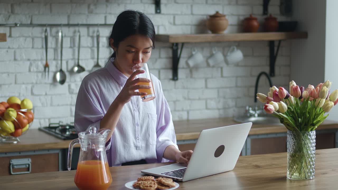 Asian woman sit at table in cozy kitchen working at laptop computer ...