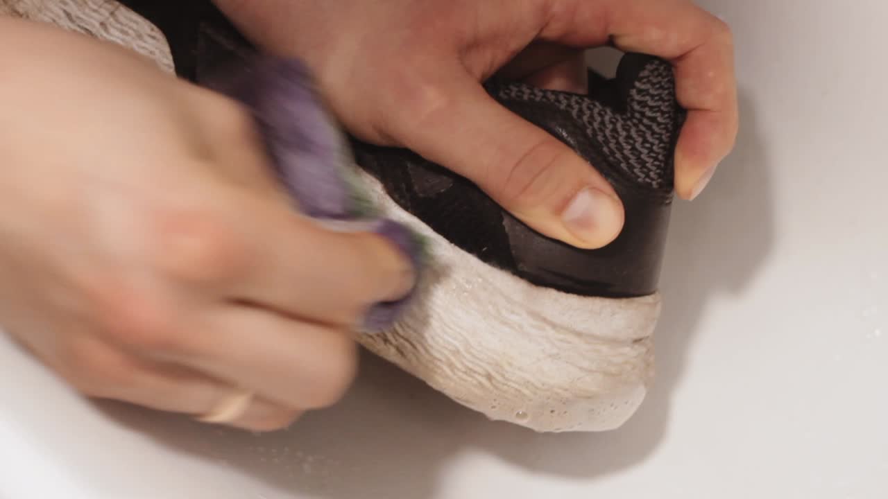 Caucasian hands washing and scrubbing the sole of training shoes with a ...