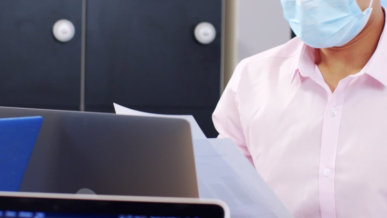 Young man in face mask looking at papers in modern office Free Stock ...