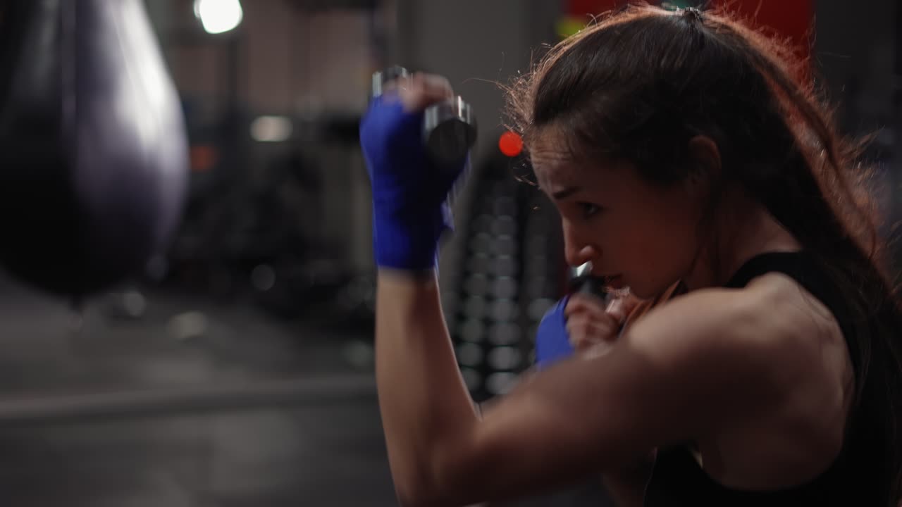 Free stock video - Female boxer strikes using dumbbells at boxing gym