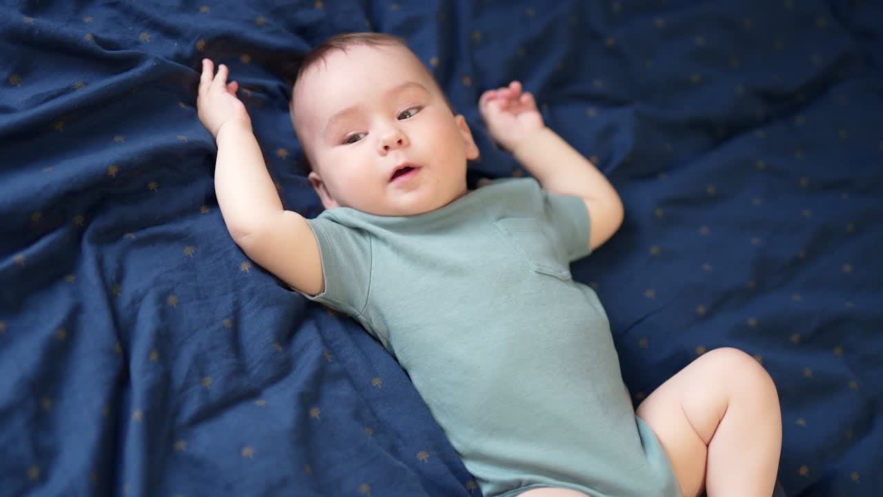 Lovely baby being very active lying on bed. Adorable kid waving legs ...