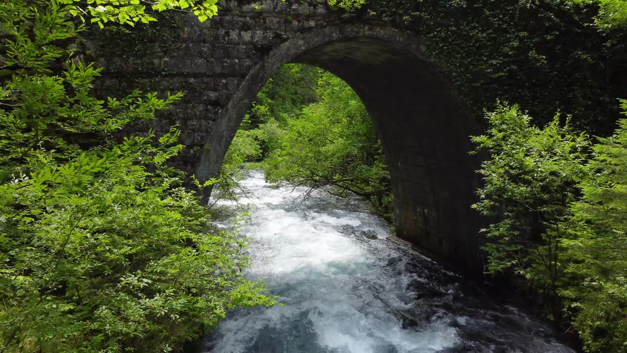 Premium stock video - Old stone arch bridge over river in lush green forest