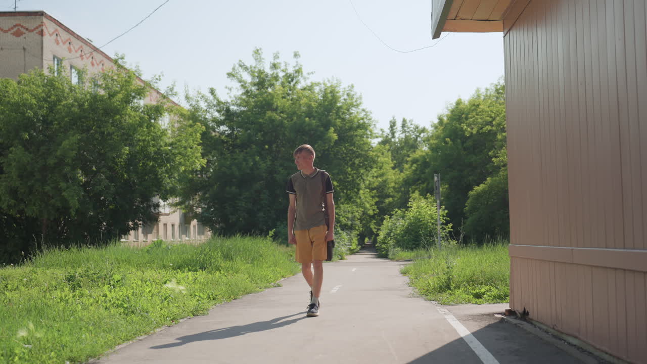 Lone Man Walking Along Sunlit Path, Carrying Satchel Past Building And ...