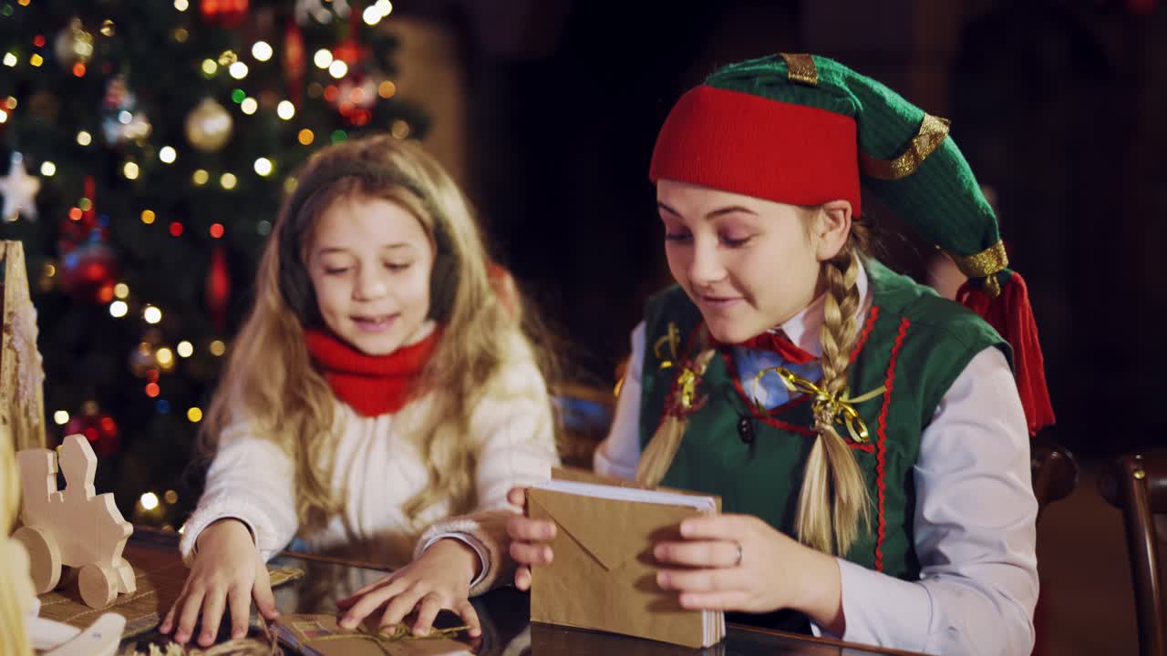A funny elf is sitting at the table with a little girl and showing how ...