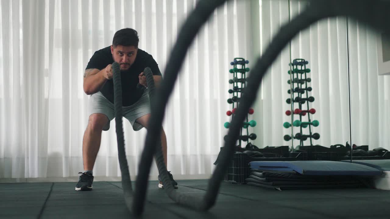 Premium stock video - Man using battle ropes for whipping exercise in a gym