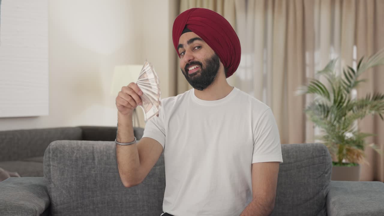 Premium stock video - Egoistic sikh indian man using money as fan