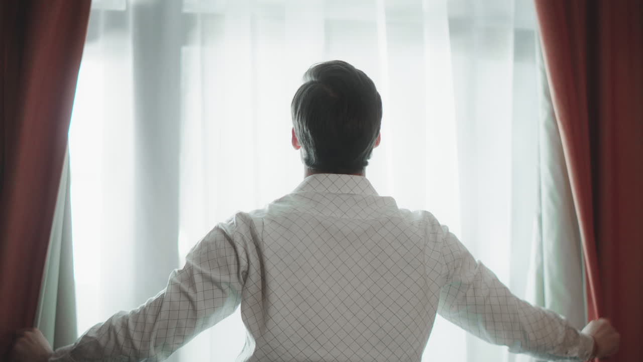 Premium stock video - Back view of young man opening curtains closeup ...