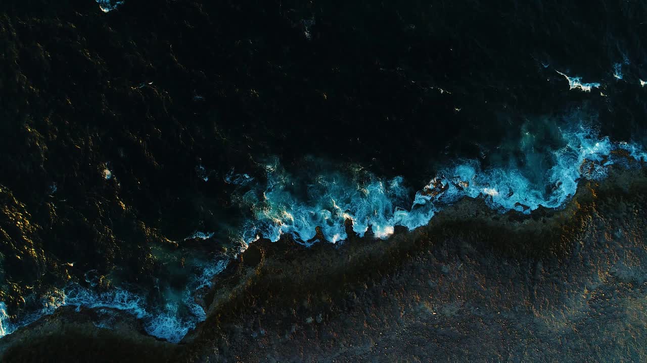 Aerial top down perspective as whitewash ocean waves crash on rocky ...
