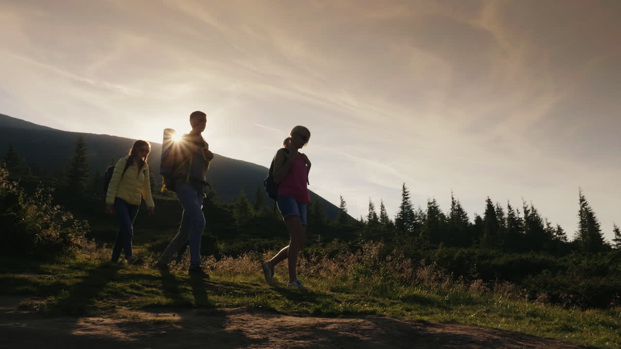 A group of friends with backpacks rises up the mountain in the rays of ...