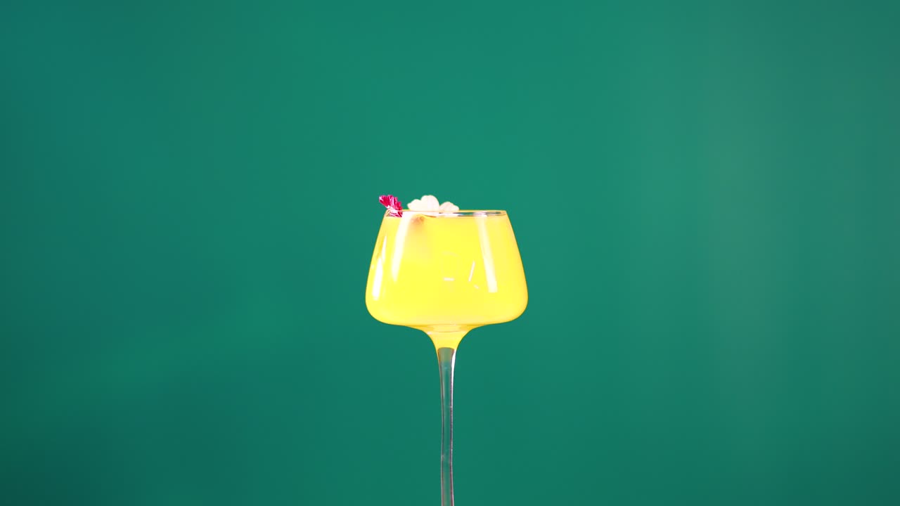 A vibrant yellow cocktail with garnish against a green screen backdrop ...