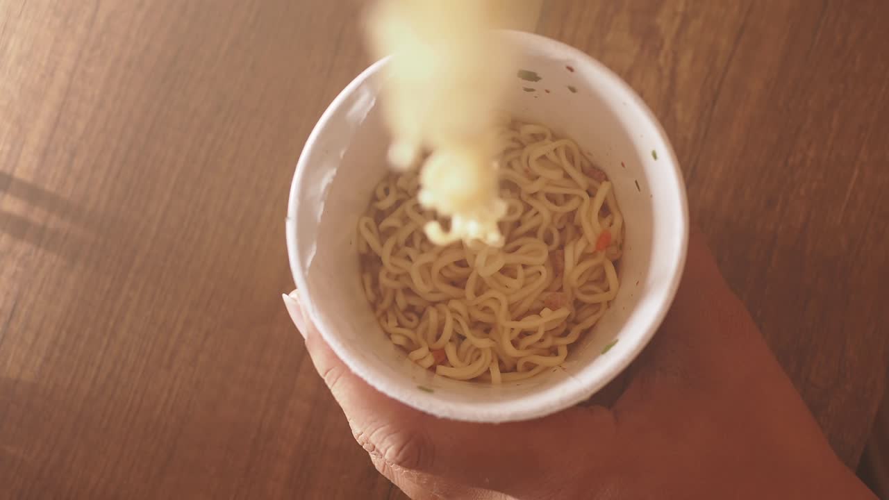 Premium stock video - Pouring hot water into cup of ramen noodles