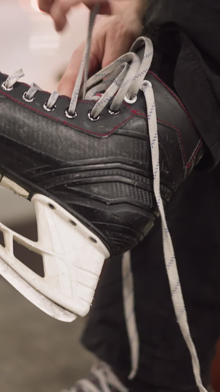 A close-up view of someone loosening the laces of a black ice skate ...