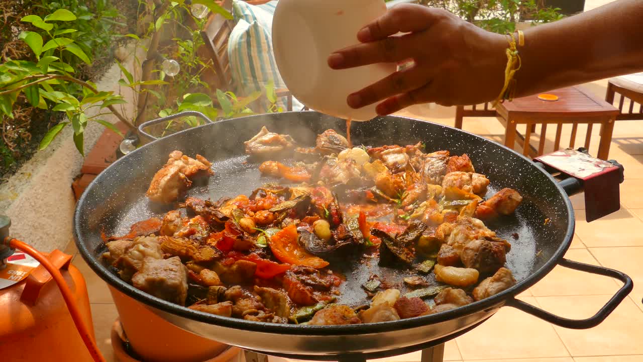 Seasoning the chicken and vegetables in a pan for paella, traditional ...