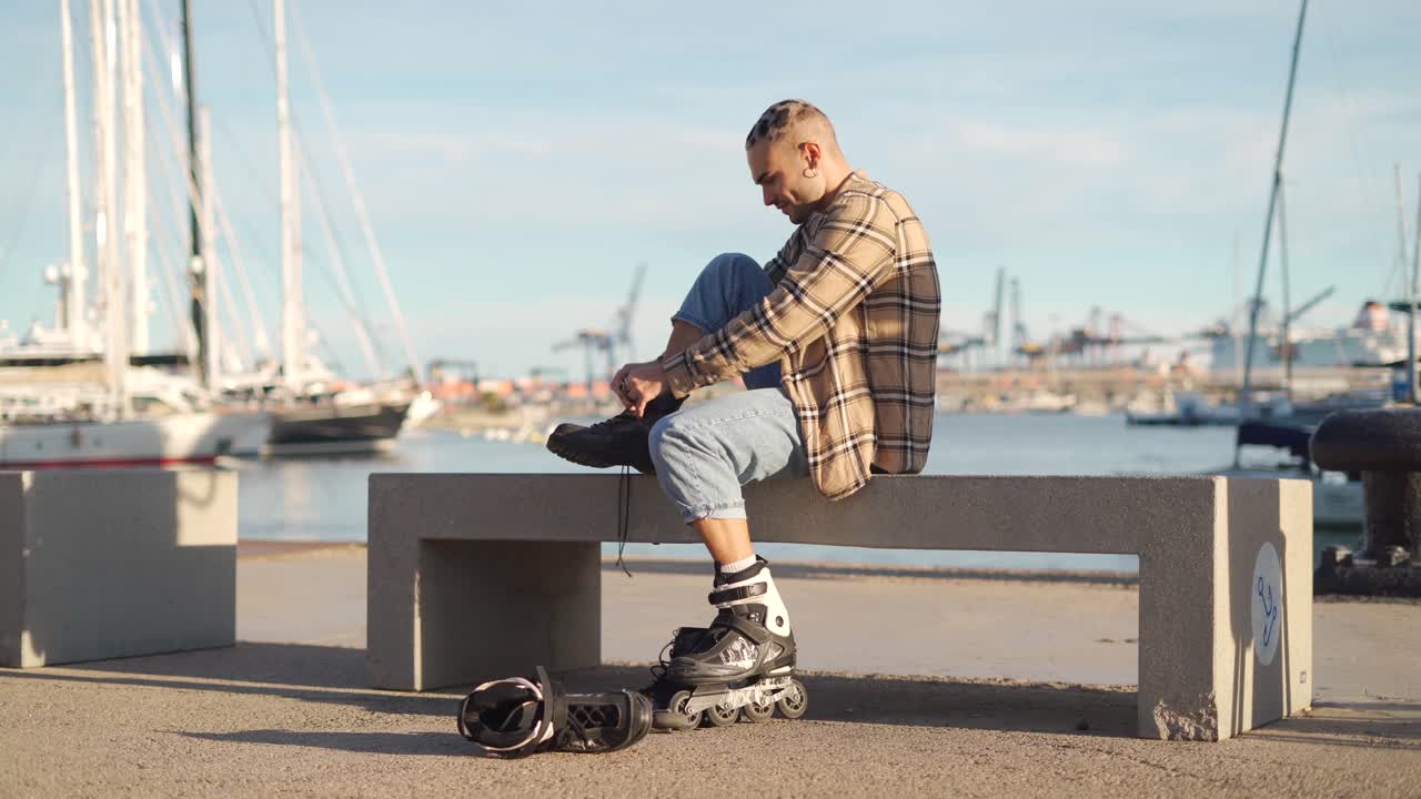 Premium stock video - Stylish man putting on roller skates on embankment