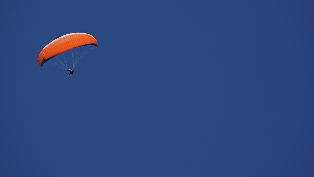 An orange parachute floats in a blue sky in the middle of the day ...