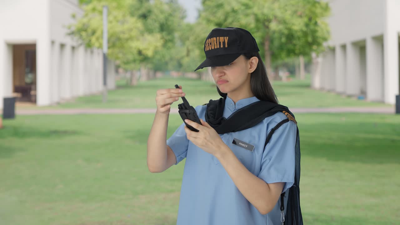 Confused indian female security guard trying to fix walkie talkie ...
