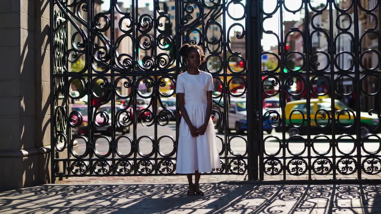 Young woman in a white dress stands serenely at an ornate wrought iron ...