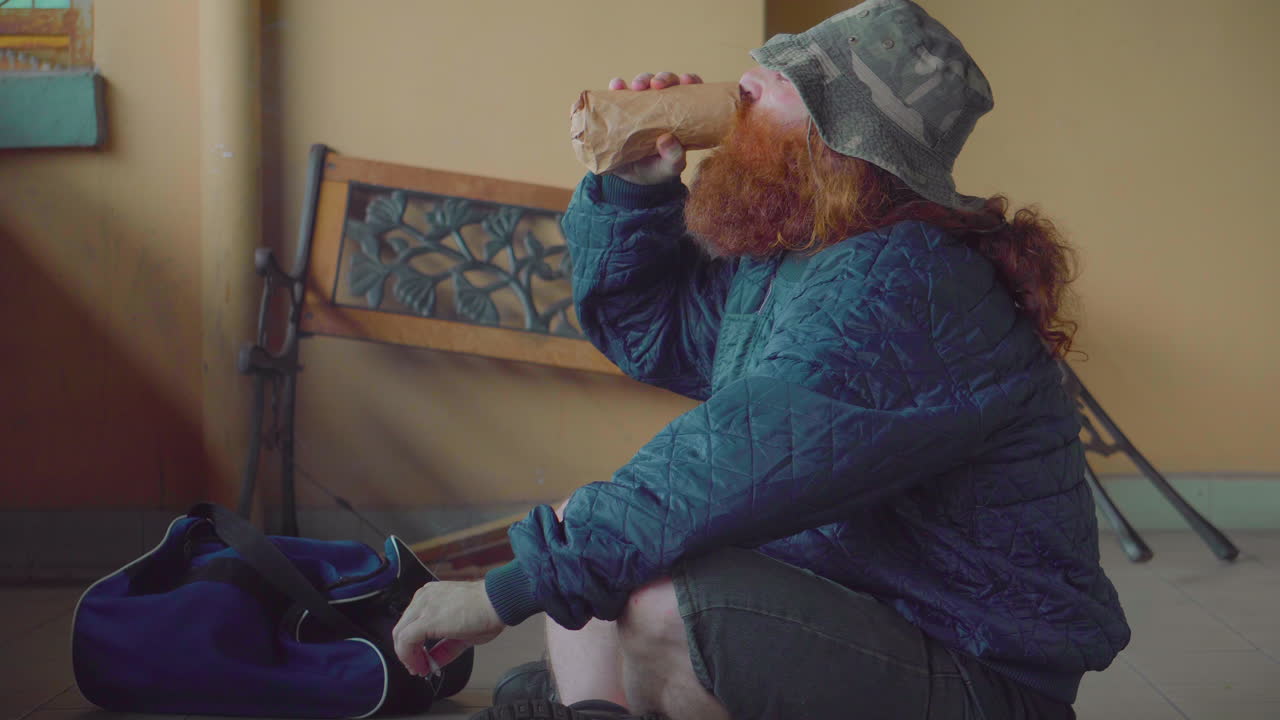 Homeless man outdoors near broken bench lighting up a marijuana or ...