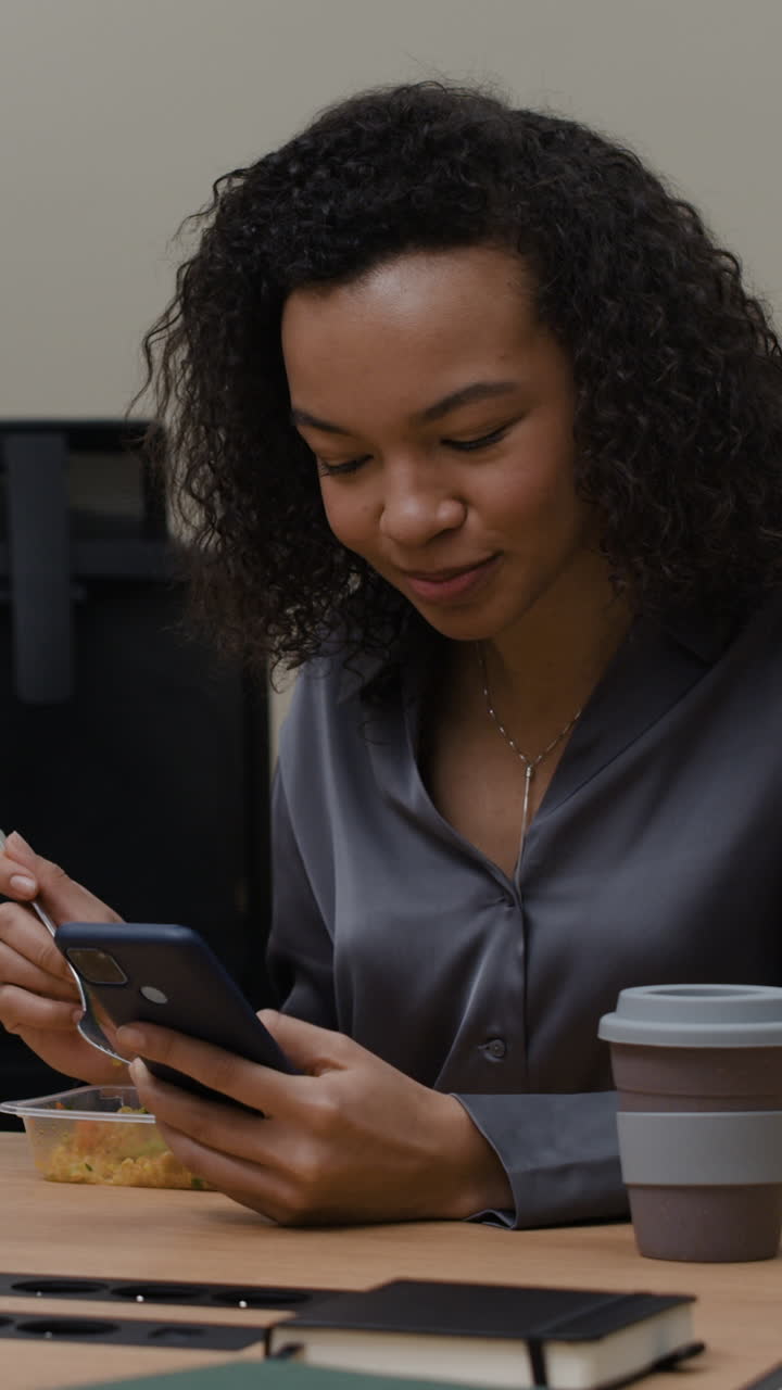 A woman using a mobile phone during her lunch break at the office ...