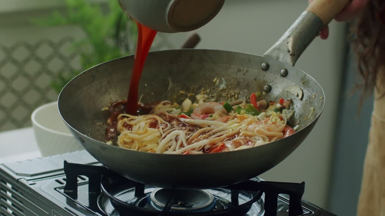 Woman pouring broth into pan with wok noodles Premium Stock Video Footage