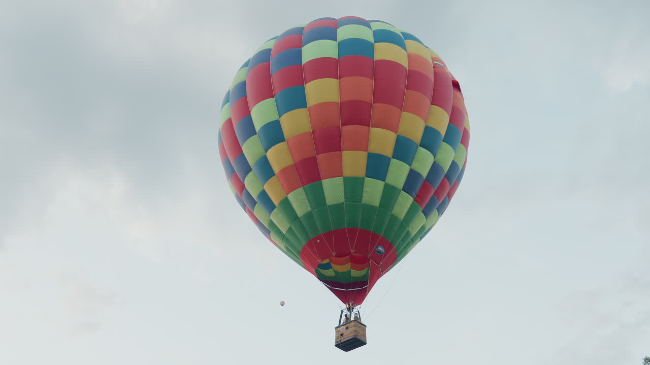 Travellers in colorful hot air balloon drifting across serene open ...