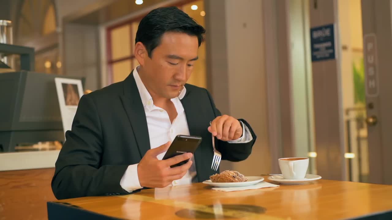 Premium stock video - Businessman having food while using mobile phone 4k
