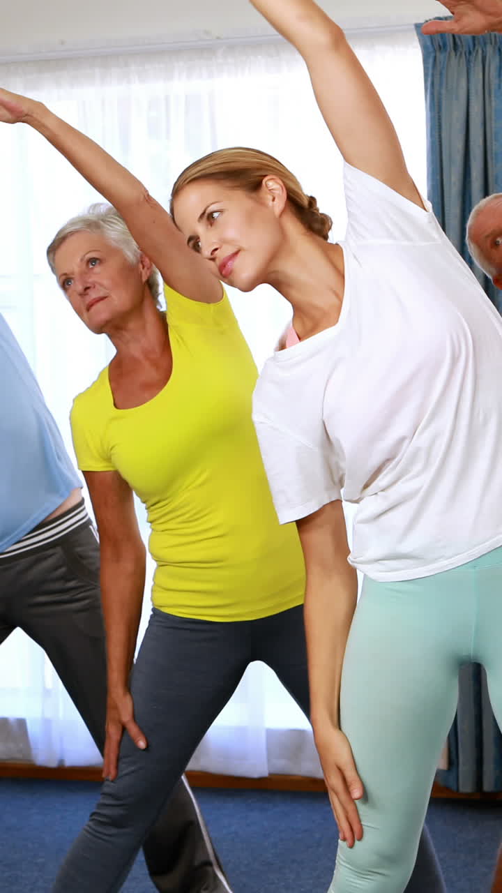 Trainer assisting senior citizens in performing stretching exercise ...