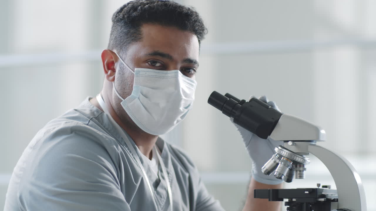 Premium stock video - Portrait of male doctor in mask using microscope