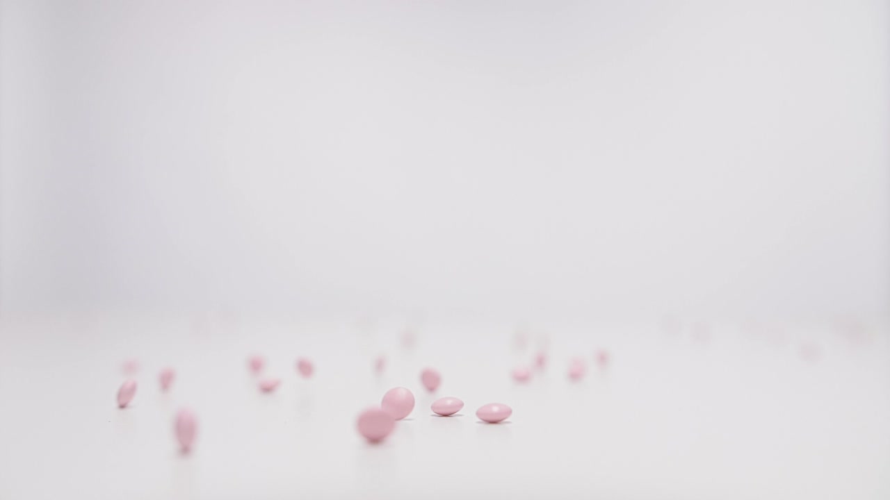 Premium stock video - Rose pills falling on white background in slow motion