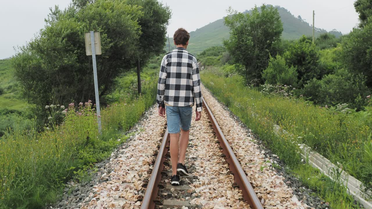 Teenage boy walking on train tracks in nature Premium Stock Video Footage