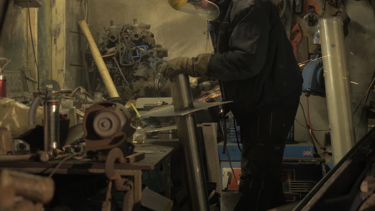 Man in messy workshop angle grinding steel plate on stainless steel ...