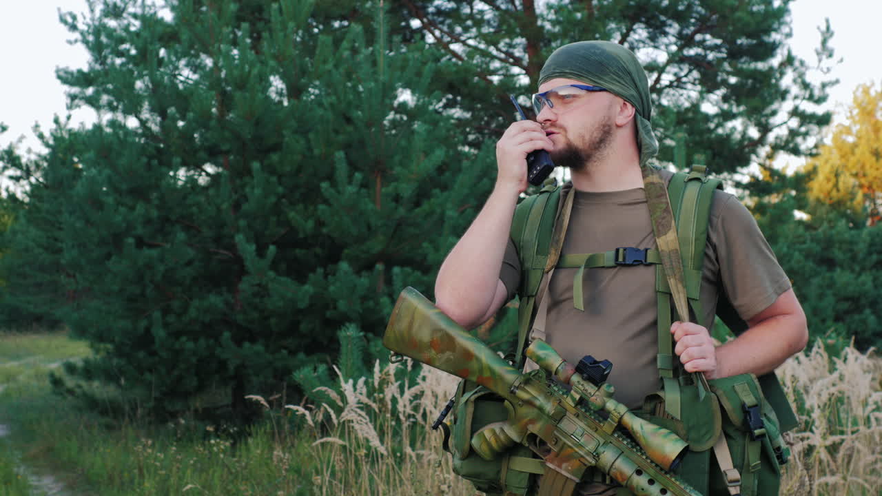 Premium stock video - Man in camouflage with guns speaking on the radio