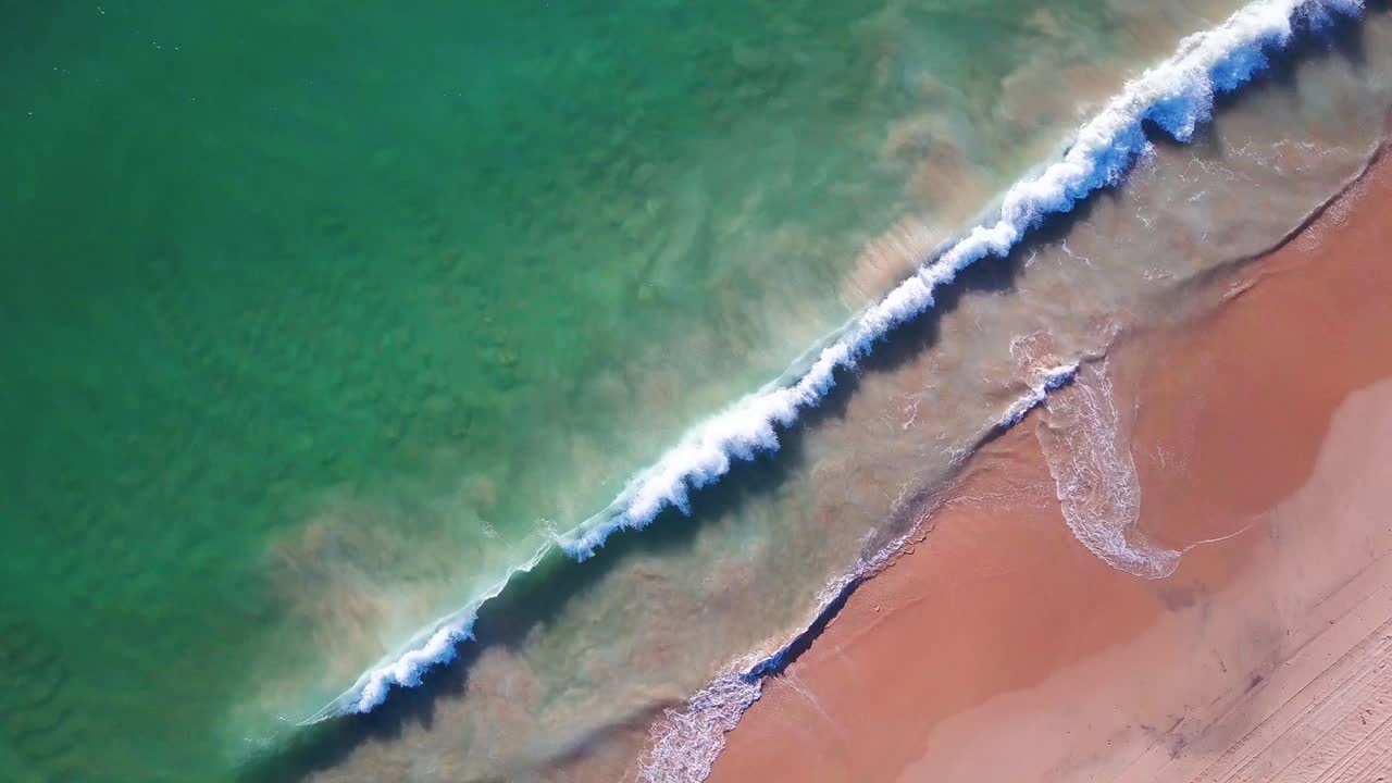 Aerial overhead ascending shot of big waves reaching the beach ...